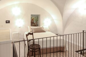 Quarto com uma cama, uma cadeira, um quadro e duas luzes na parede.
