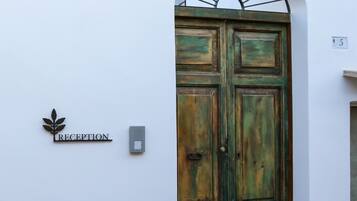 Uma porta de madeira verde com um arco de metal acima, uma placa de recepção e um pequeno número '5' na parede.