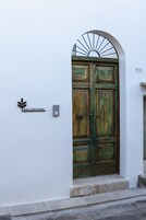 Uma porta de madeira verde com um arco de metal acima, uma placa de recepção e um pequeno número '5' na parede.