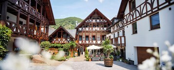 Um pátio europeu tradicional com edifícios de estrutura de madeira, mesas ao ar livre e plantas em vasos.