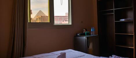 Quarto de hotel com cama, janela com vista para uma pirâmide, minibar e guarda-roupa.