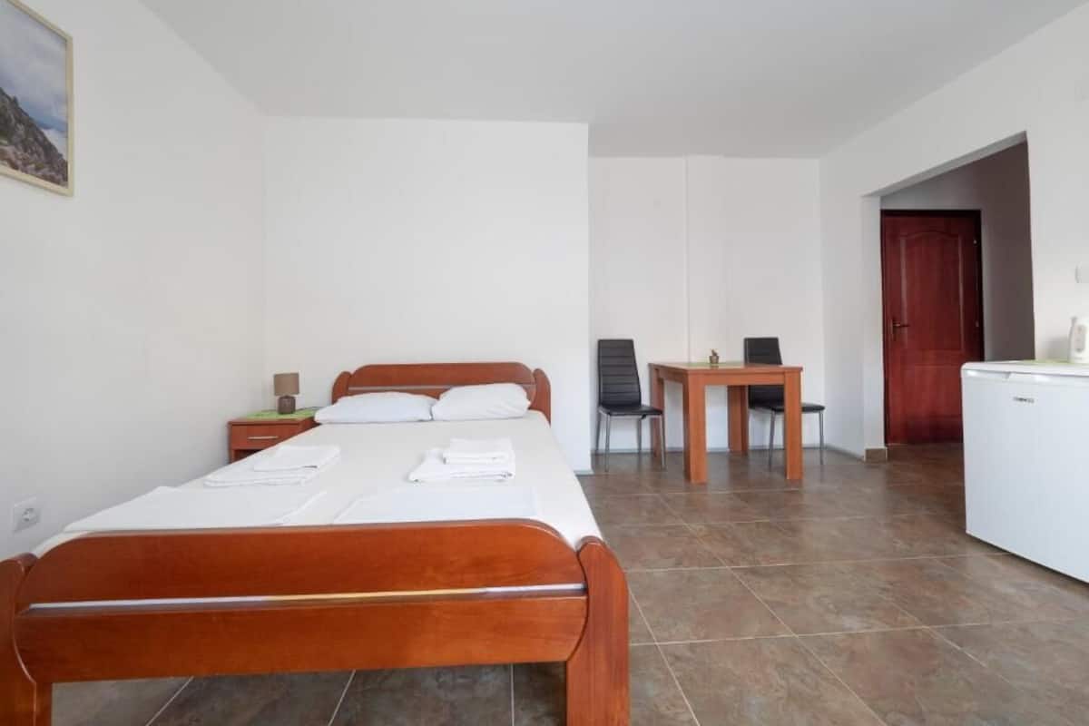 Um quarto com uma cama de madeira, uma escrivaninha, uma cadeira e uma geladeira branca.