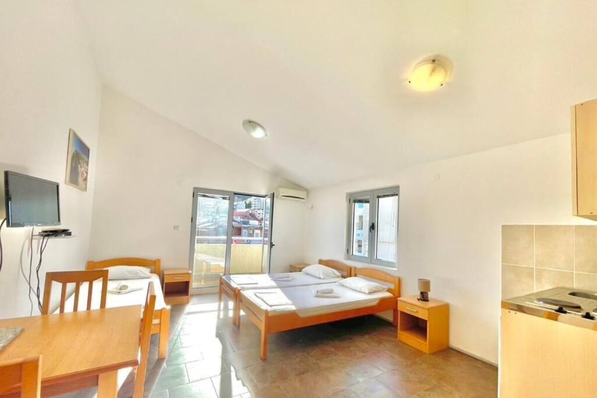 Quarto espaçoso com uma cama grande, uma escrivaninha e uma cadeira, pequena cozinha e vista através de uma janela ampla.