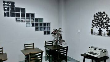 Um quarto com uma mesa de jantar, cadeiras, um vaso com planta, uma máquina de escrever e uma parede com padrão geométrico e um enfeite de árvore.