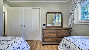Quarto com duas camas, cômoda, espelho e janela com cortinas.
