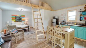 Quarto estilo loft com escada de madeira, uma cama, uma obra de arte colorida na parede e uma pequena cozinha compacta com armários verde-água.