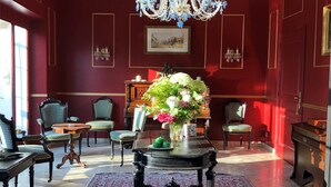 Um quarto com um candelabro, uma mesa com um vaso de flores e várias cadeiras.