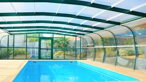 Piscina coberta com estrutura de vidro, rodeada por uma moldura de metal verde, e vista para o exterior através do vidro.
