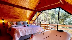 Quarto de cabana de madeira com uma cama grande, uma banheira e uma janela com vista para uma floresta.