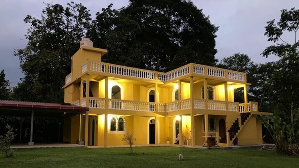 Um edifício amarelo de dois andares com varanda, janelas em arco e escadaria.
