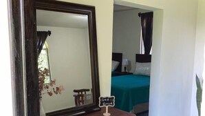 Quarto de hotel com um espelho grande, uma mesa pequena com uma placa e uma cama com cobertura azul.