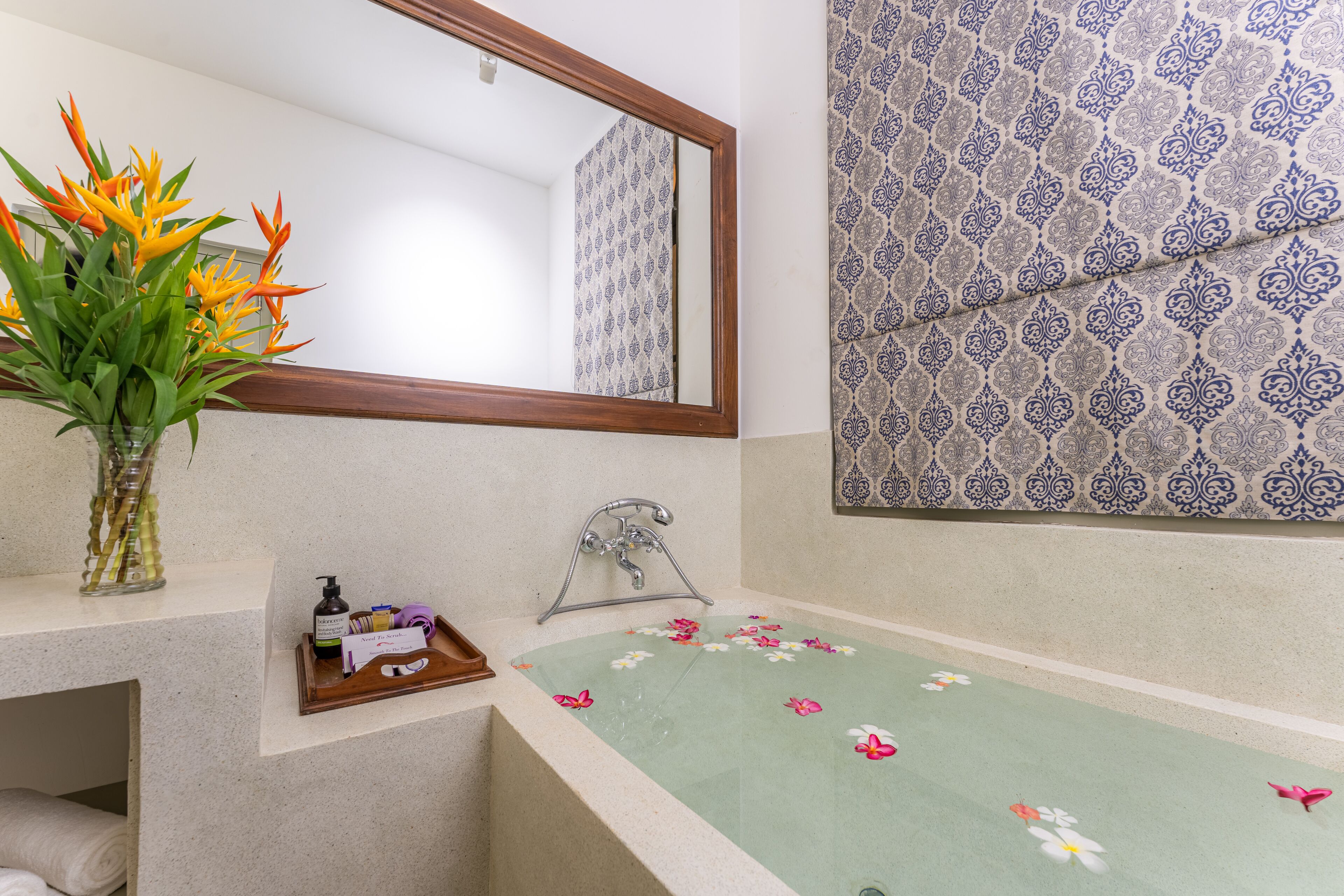 Um banheiro com banheira, espelho, vaso com flores e porta-toalhas.