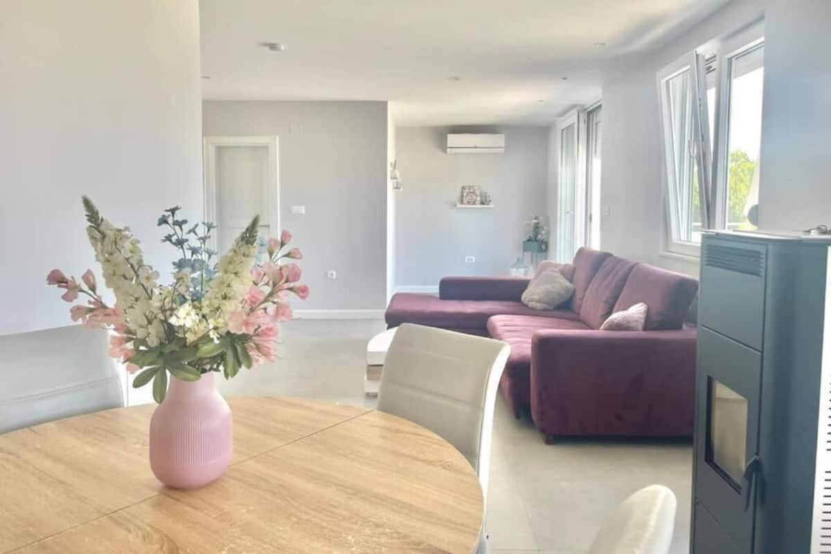 Uma sala de estar moderna com um sofá, uma mesa de jantar com um vaso rosa e uma lareira.