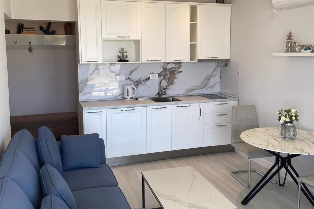 Uma cozinha moderna com armários brancos, bancada de mármore e área de refeições com mesa redonda e sofá azul.