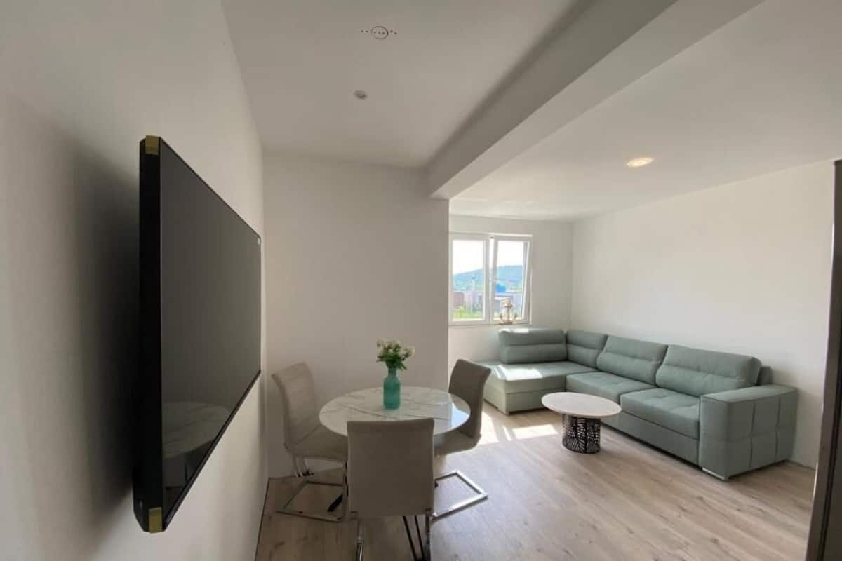 Uma sala de estar moderna com uma televisão de tela plana, uma mesa de jantar redonda e um sofá seccional verde.