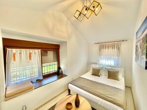 Quarto com cama, janela com cortinas, mesa pequena com um vaso e luminária no teto.