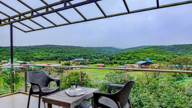 Uma varanda com mesa e cadeiras, com vista para uma paisagem verde e exuberante.