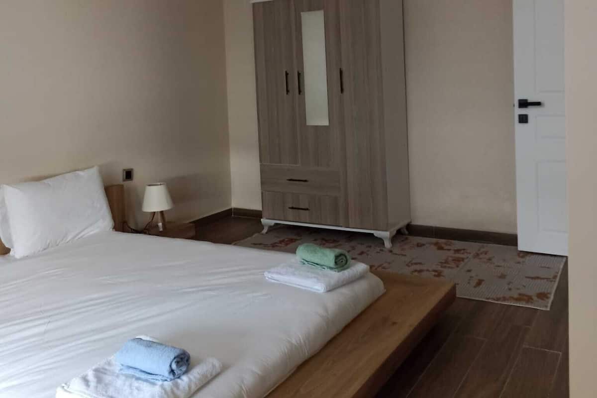 Quarto com cama grande, guarda-roupa, mesa de cabeceira e uma porta.