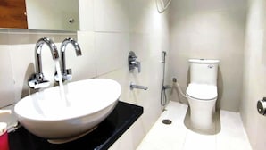 Casa de banho moderna com lavatório branco, duas torneiras, espelho, sanita e chuveiro.