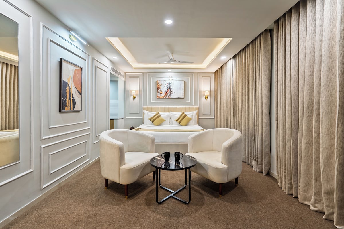 Quarto de hotel com uma cama, duas poltronas, uma mesinha e obras de arte nas paredes.