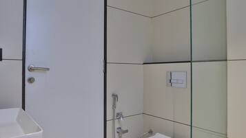 Uma casa de banho moderna com cabine de duche em vidro, sanita branca e lavatório com bancada preta.