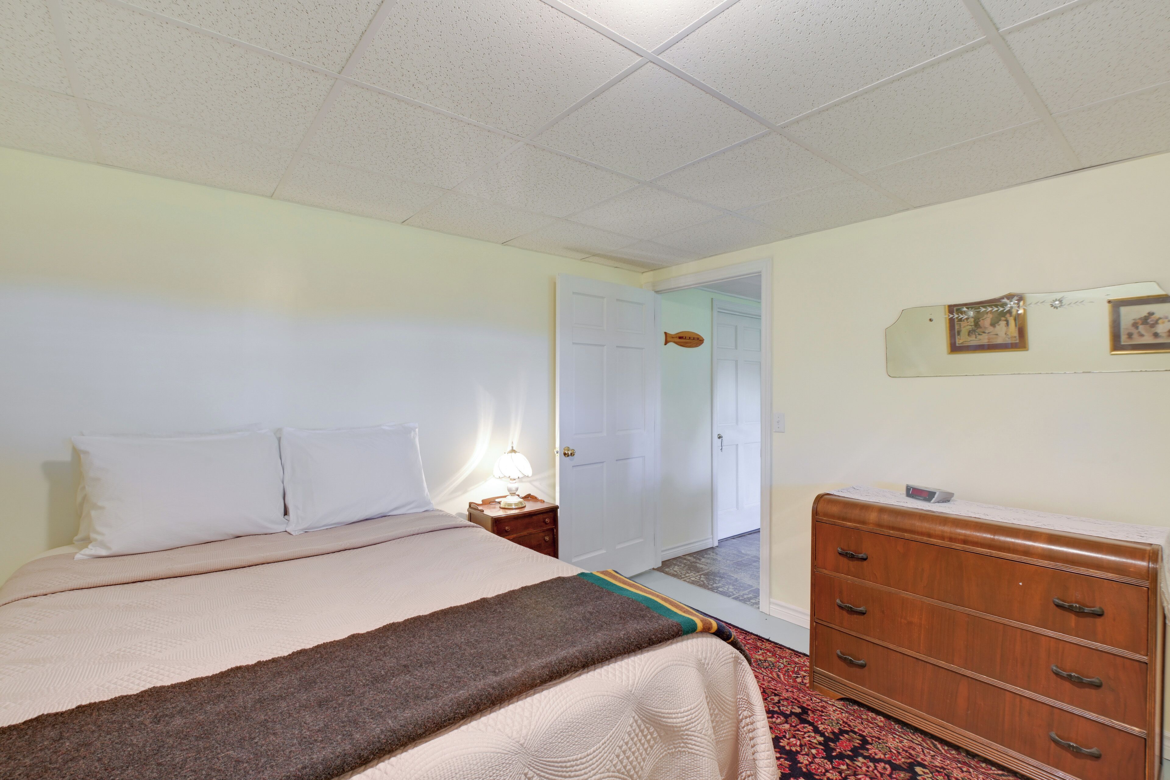 Quarto de hotel com cama, mesa de cabeceira, cômoda e porta que dá para outro espaço.