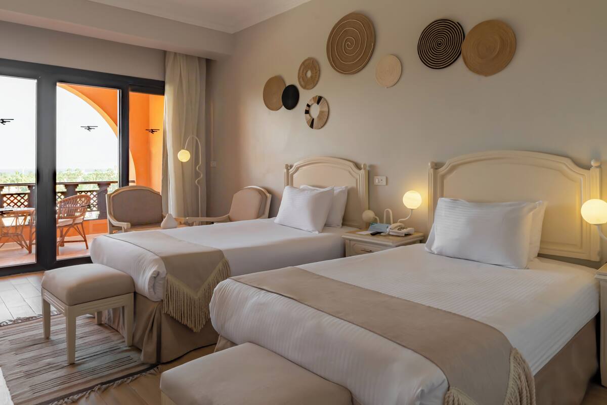 Quarto de hotel com duas camas, varanda com vista e arte decorativa na parede.