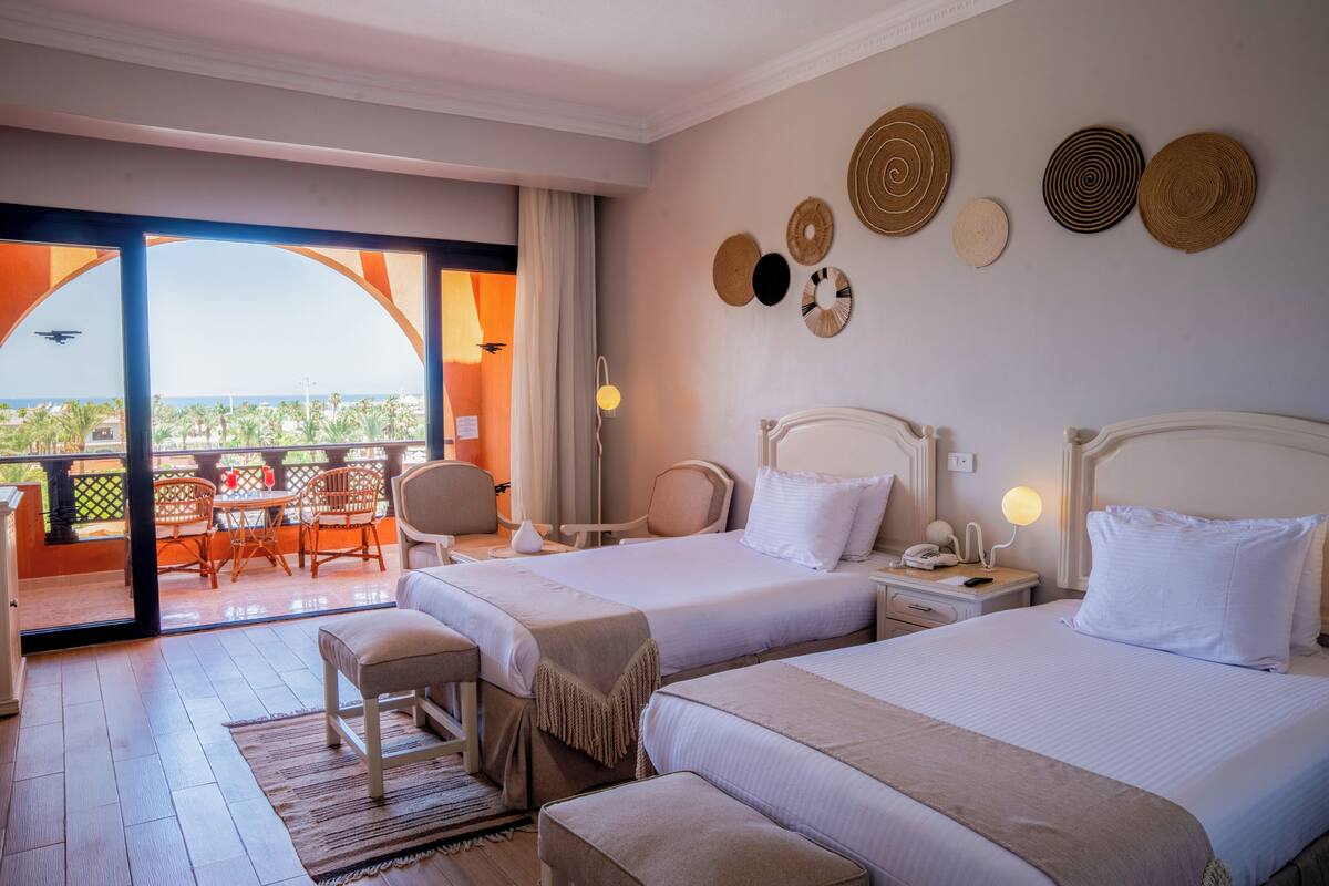 Quarto de hotel com duas camas, varanda com cadeiras e decoração na parede.