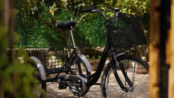 Uma bicicleta ergométrica com cesto, estacionada em um caminho de pedras.