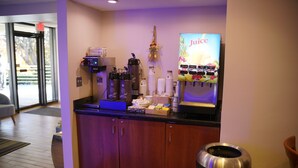 Uma área de recepção com dispensador de suco, máquina de café e lixeira.