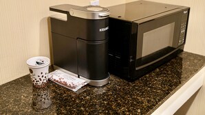 Uma máquina de café e um micro-ondas em uma bancada de granito.