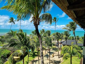 Um resort tropical com palmeiras, vista para a praia e uma estrutura com telhado de palha.