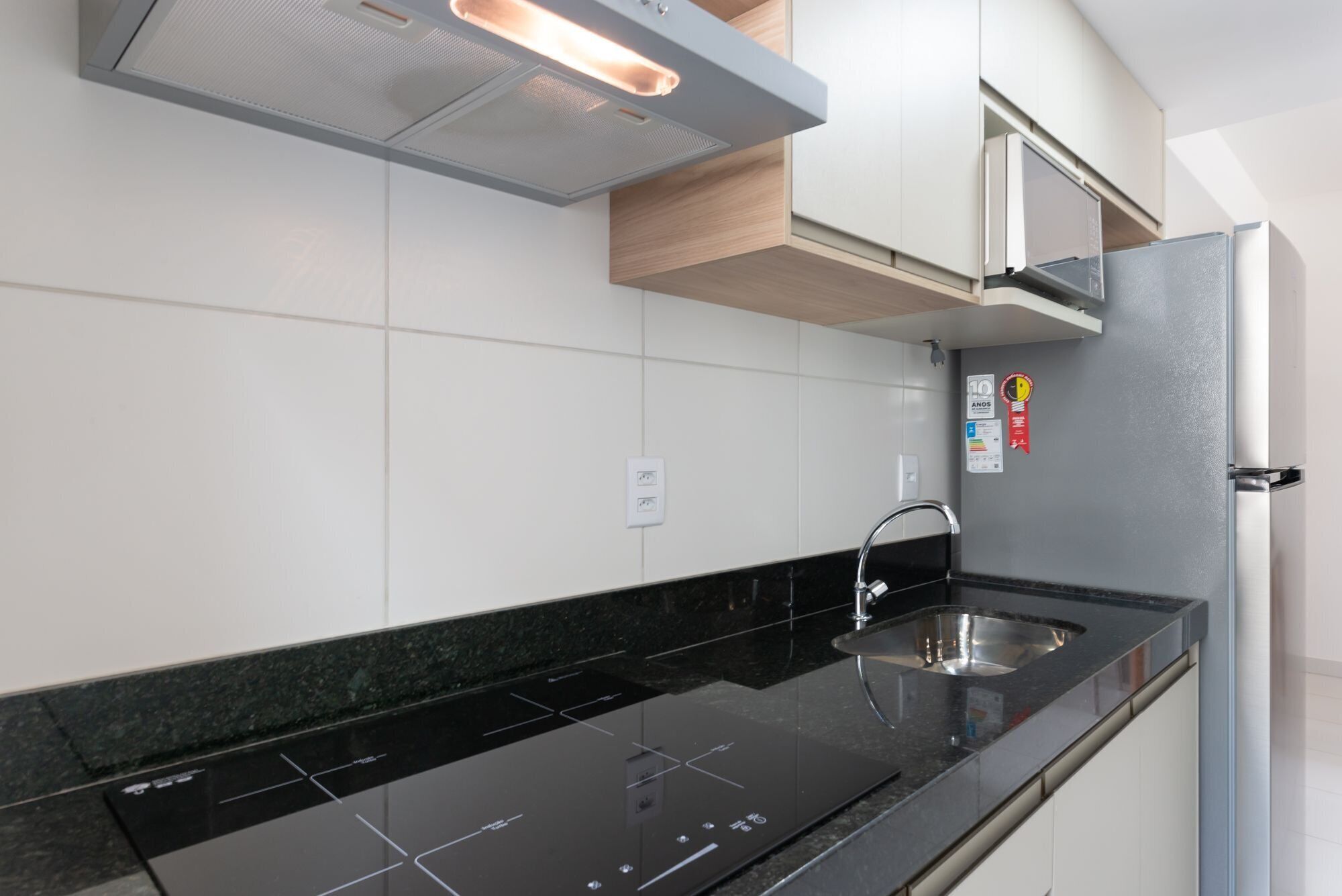 Uma cozinha moderna com bancada preta, pia de aço inoxidável e forno embutido.
