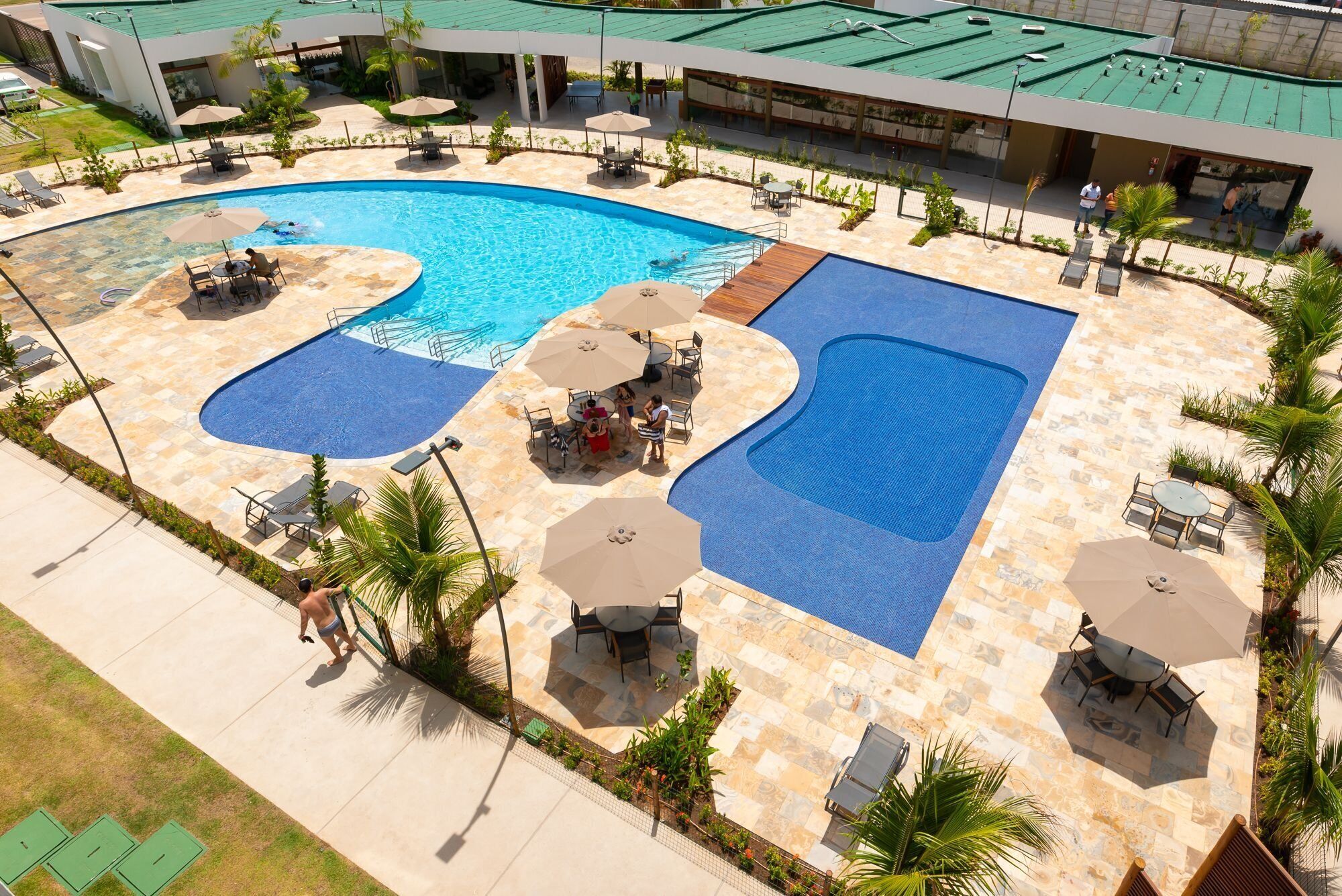 Uma grande piscina ao ar livre com várias áreas, rodeada por espreguiçadeiras e guarda-sóis.