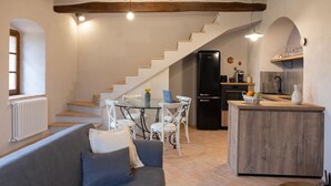 Uma cozinha moderna com geladeira preta, ilha de madeira e área de jantar com mesa de vidro e cadeiras brancas.
