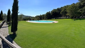 Um gramado bem cuidado com uma piscina circular, rodeado por árvores e um muro de pedra.