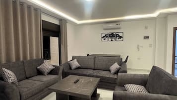 Uma sala de estar moderna com sofás cinza, uma mesa de centro de mármore e uma luminária no teto.