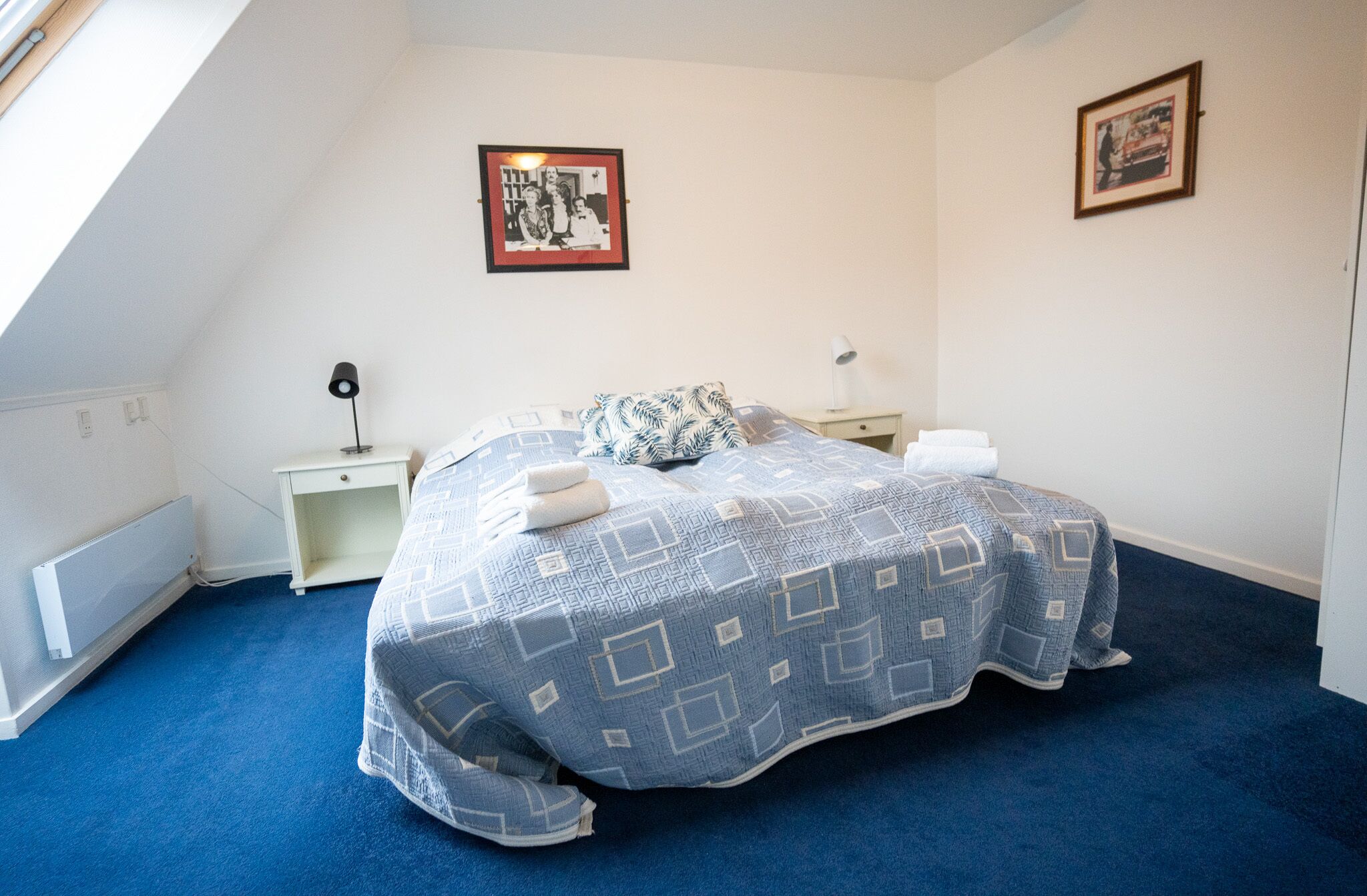Quarto com cama, mesa de cabeceira, luminária e quadro pendurado na parede.