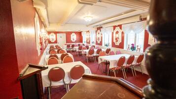 Uma sala de banquetes com fileiras de mesas e cadeiras, paredes brancas e detalhes em vermelho.