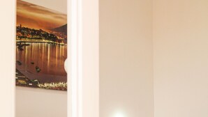 Quarto de hotel com uma cama, uma mesa de cabeceira com abajur e um quadro de uma vista urbana na parede.