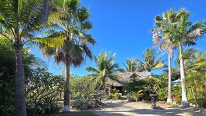 Um jardim tropical com palmeiras, uma cabana com telhado de palha e um caminho de pedra.