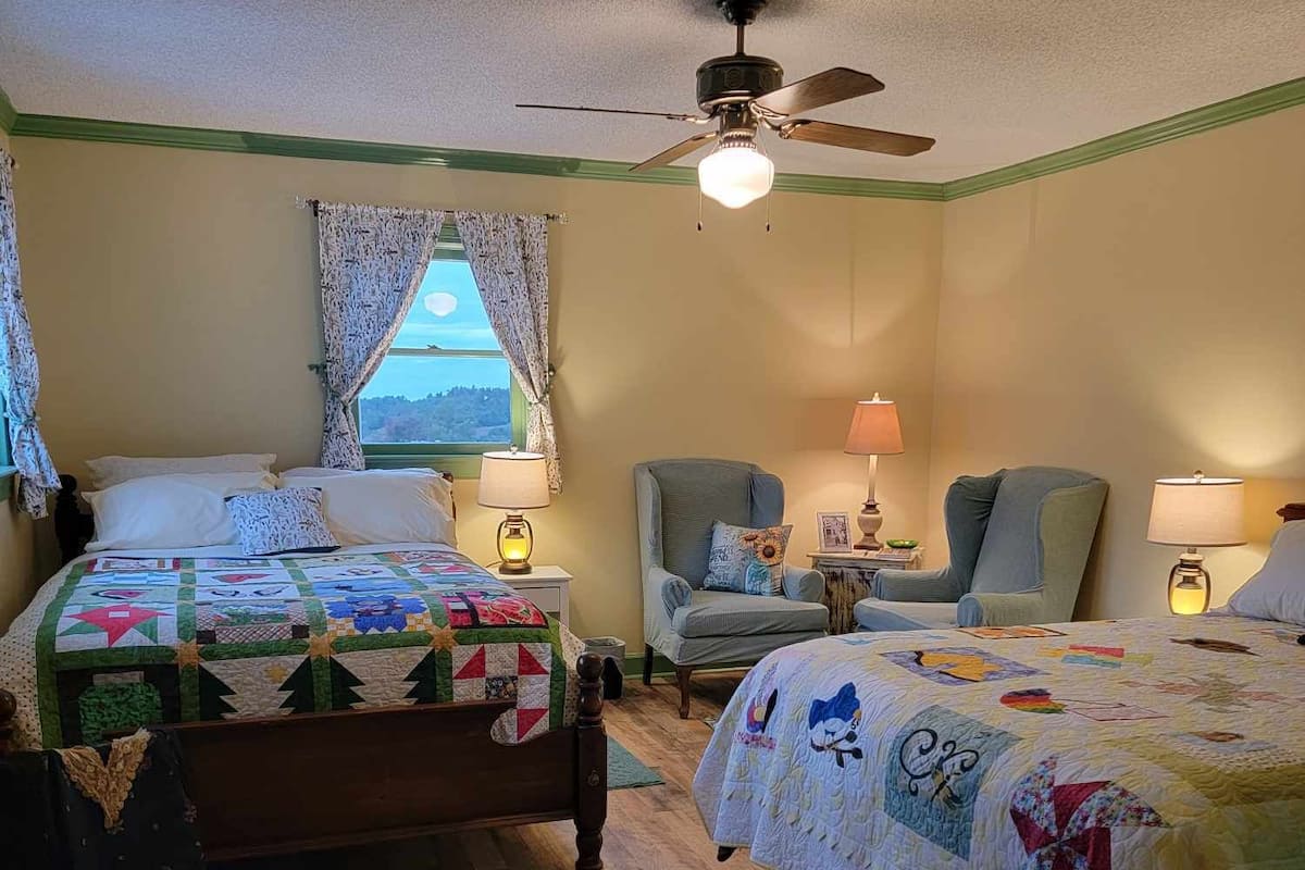 Quarto com duas camas, ventilador de teto e janela com cortinas.