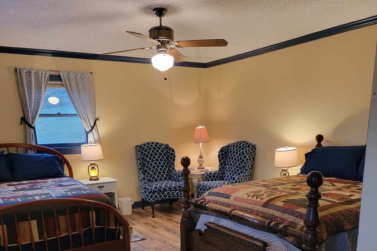 Quarto com duas camas, um ventilador de teto e uma janela com cortinas.