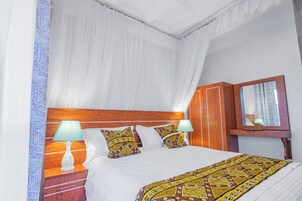 Quarto com cama de dossel, cabeceira de madeira, luminárias de cabeceira, almofadas estampadas e mesa de cabeceira.