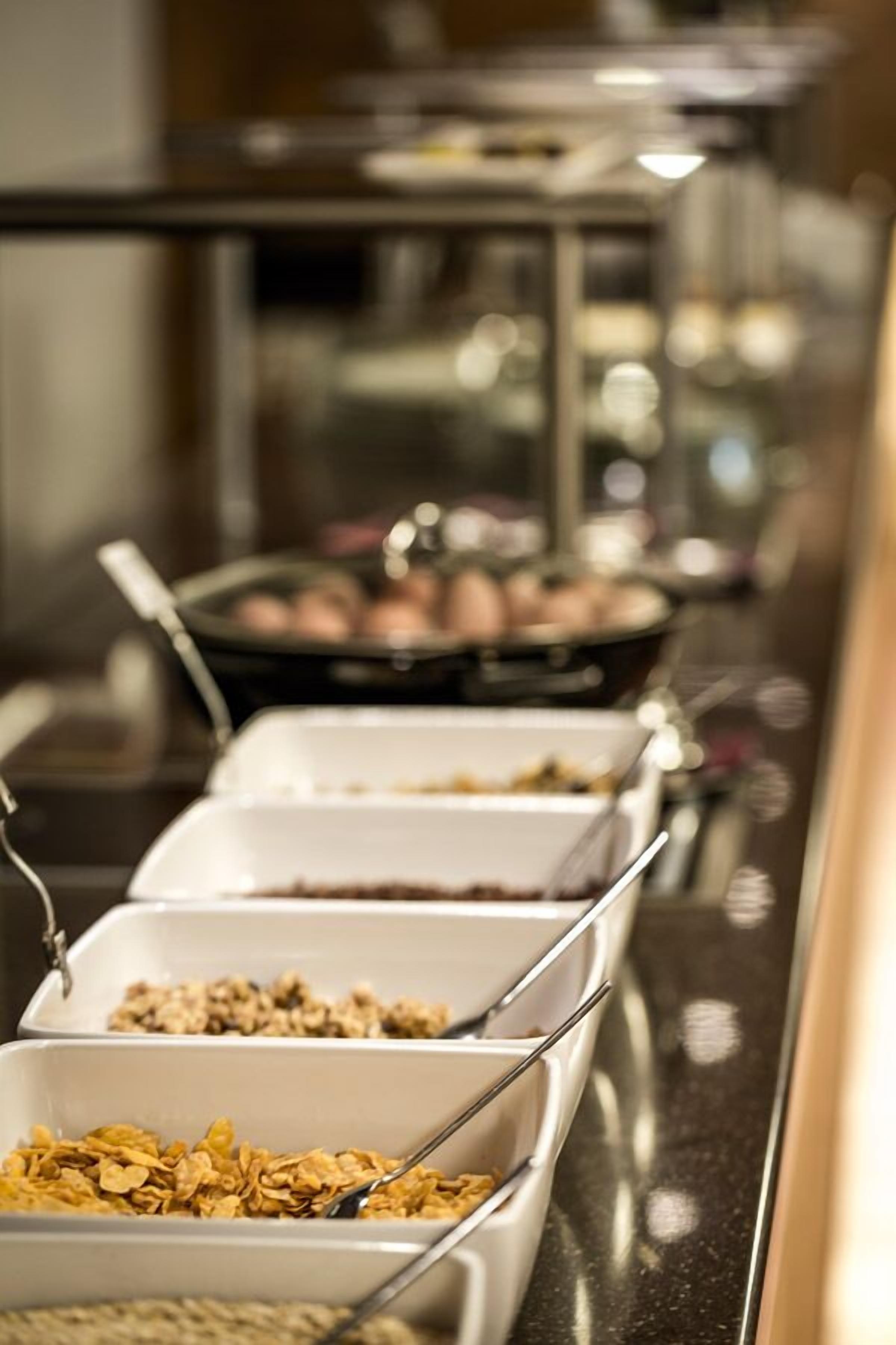 Buffet com diversos alimentos, incluindo cereais e ovos, em ambiente interno bem iluminado.