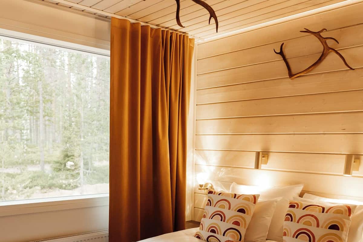 Quarto com cama grande, janela com cortinas e teto de madeira com luminária original.
