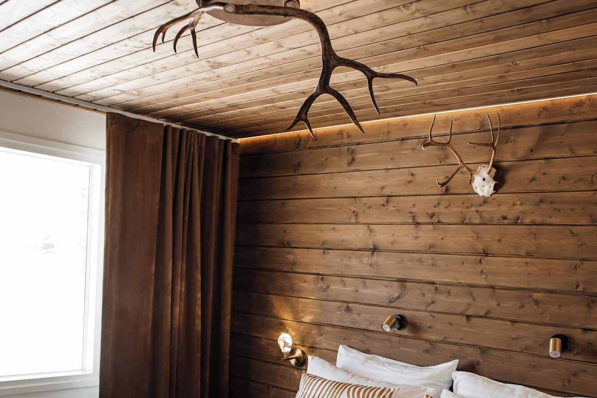 Quarto com teto de madeira, cama com almofadas listradas e cabeceira com chifres.