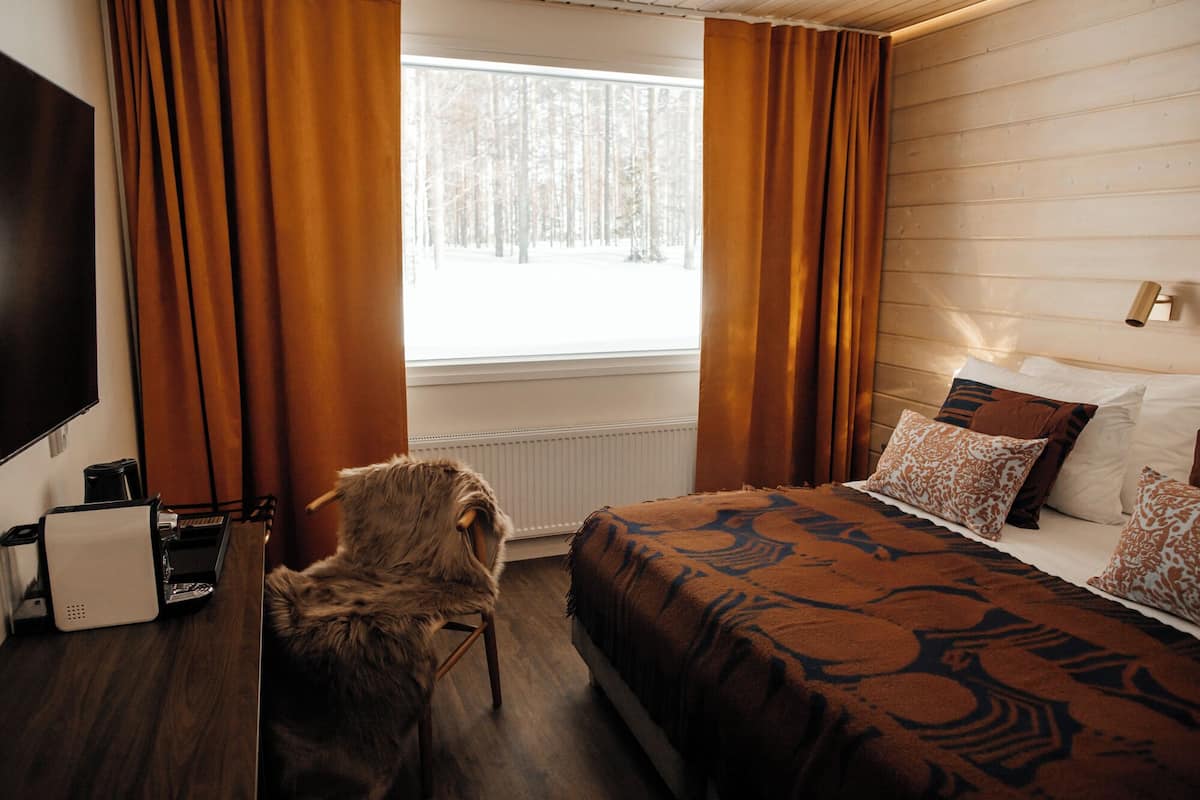 Quarto de hotel com uma cama, uma cadeira, uma televisão e uma janela com cortinas.