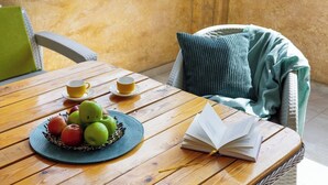 Uma mesa de madeira com um descanso trançado, um prato de maçãs, duas xícaras amarelas e um livro aberto.