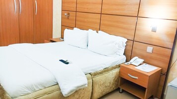 Quarto de hotel com cama, mesa de cabeceira, telefone e jornal, e guarda-roupa.
